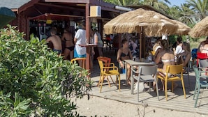 Um bar à beira-mar com mesas ao ar livre e guarda-sóis de palha.