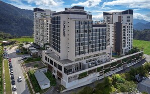 Um hotel moderno de vários andares com um pátio central, rodeado por vegetação exuberante e montanhas ao fundo.