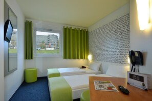 Quarto de hotel com duas camas, uma escrivaninha, um telefone e uma janela com cortinas.