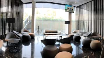 Um lobby moderno com teto curvo, parede de vidro e área de estar com cadeiras e pufes contemporâneos.