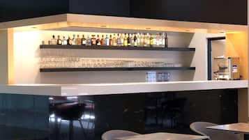 Uma área de bar moderna com bancada preta, prateleiras cheias de garrafas de bebidas e vários bancos.