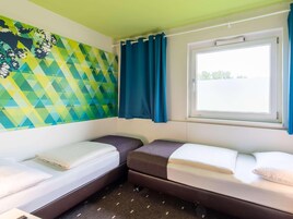 Quarto com duas camas, janela com cortinas e um design geométrico colorido na parede.