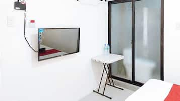 Quarto de hotel com cama, uma pequena mesa com cadeira, espelho, porta de correr de vidro e uma tomada.