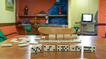 Uma mesa de madeira com dominós e uma televisão num quarto com paredes laranja e um quadro.