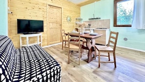 Uma sala de estar acolhedora com parede de madeira, televisão, mesa de jantar com cadeiras e um sofá estampado.