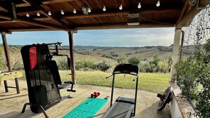 Uma academia ao ar livre com equipamentos de exercício, incluindo esteira, banco de peso e faixas de resistência, com uma paisagem deslumbrante ao fundo.