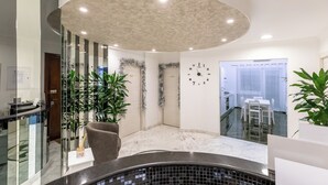 Um hall de hotel moderno, com piso de mármore, divisórias de vidro e plantas em vasos.