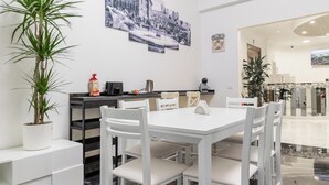 Uma zona de refeições moderna com uma mesa e cadeiras brancas, um chão de mármore preto e uma planta em vaso.