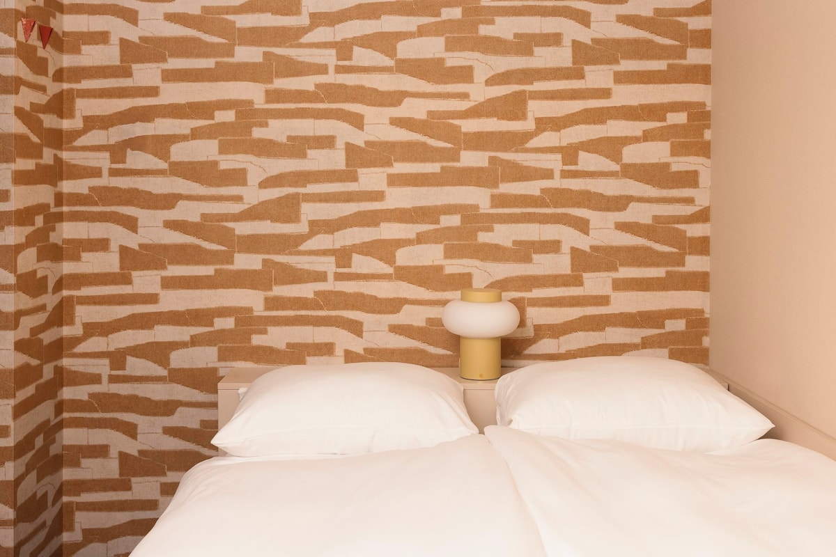 Cama bem arrumada com roupa de cama branca em quarto com parede estampada.
