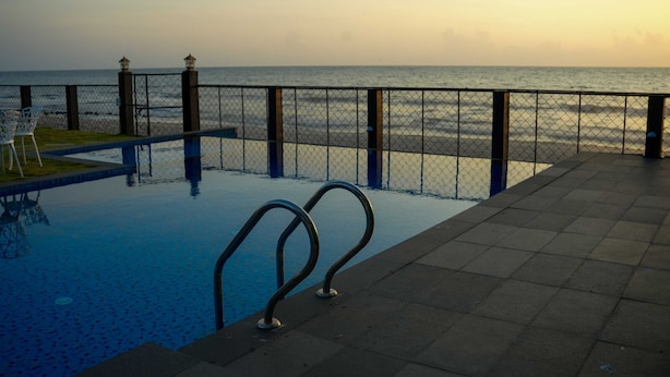 Piscina com grades de metal e vista para o mar ao pôr do sol.