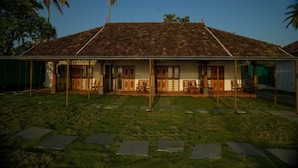 Uma casa de dois andares com telhado de telhas, varanda com cadeiras de madeira e um gramado com lajes de pedra.