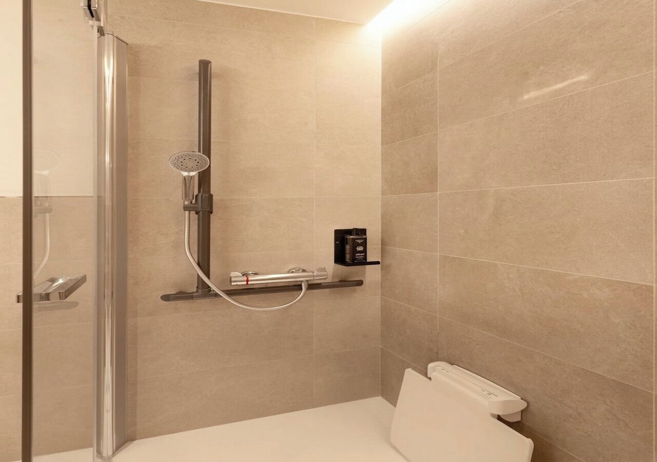 Casa de banho moderna com cabine de duche em vidro, sanita e prateleira com produtos de higiene pessoal.