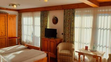 Quarto com duas camas, televisão, uma cadeira e mesa com garrafa e copos.