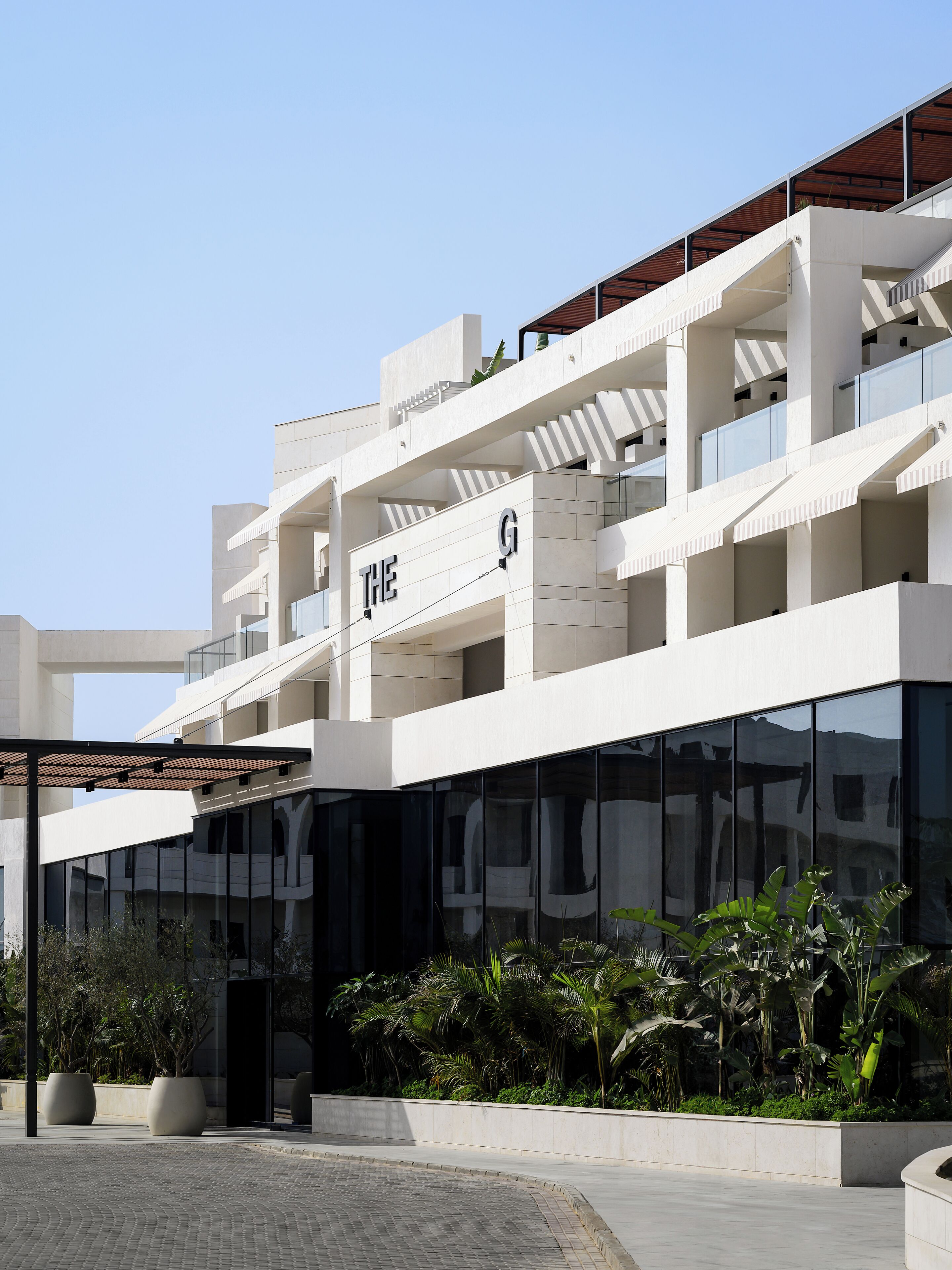 Um edifício moderno com uma placa chamativa 'THE G', com várias varandas e fachada de vidro.