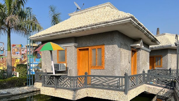 Uma casa flutuante com fachada de pedra, portas de madeira e um pequeno deck com guarda-corpo.