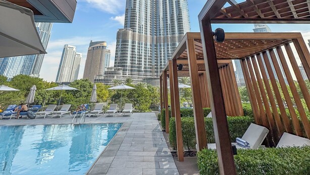 Área à beira da piscina com espreguiçadeiras e guarda-sóis, com vista para um arranha-céu imponente.