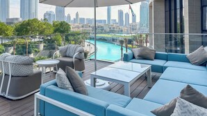 Um lounge no terraço com vista para a piscina, mobiliário moderno e paisagem urbana ao fundo.