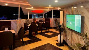 Um restaurante com piso quadriculado, paredes de mármore e uma televisão exibindo uma partida de tênis.