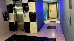 Um corredor com padrão de parede quadriculado, um elevador metálico e teto com iluminação azul.