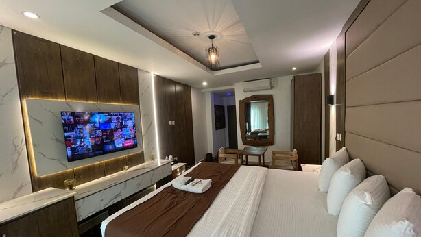 Quarto de hotel moderno com uma cama grande, televisão fixada na parede, escrivaninha e espelho.