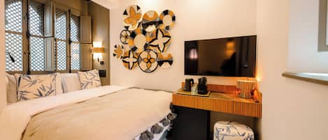 Quarto de hotel com cama, escrivaninha com televisão de tela plana, obra de arte decorativa na parede e janela com persianas.