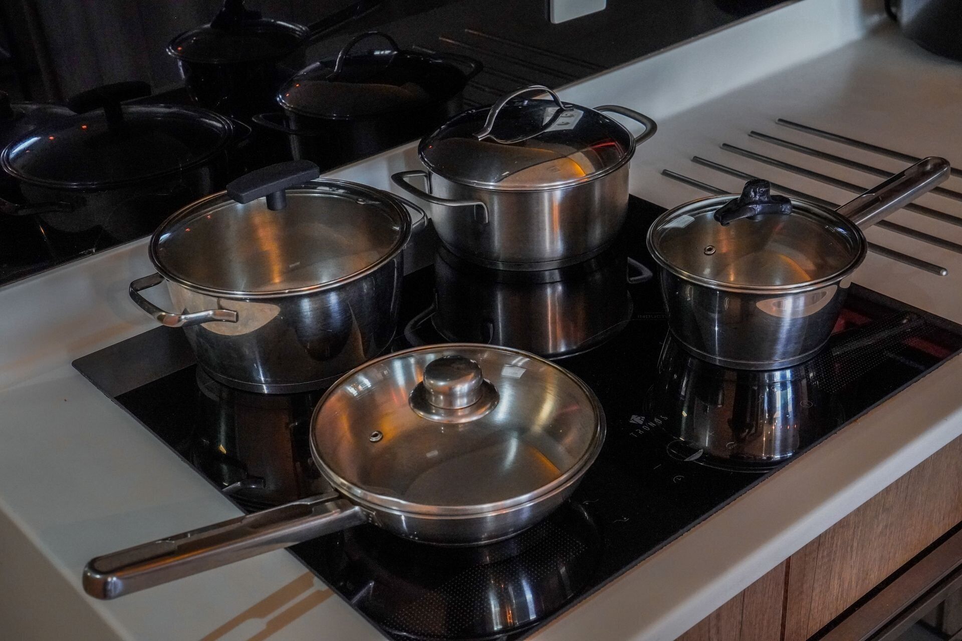 Uma cozinha com quatro panelas de aço inoxidável sobre um fogão por indução.
