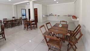 Uma área de refeições com uma grande mesa de madeira e cadeiras, piso de azulejos brancos e iluminação embutida no teto.