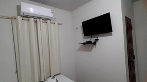 Quarto com ar condicionado branco, televisão fixada na parede e porta com puxador.
