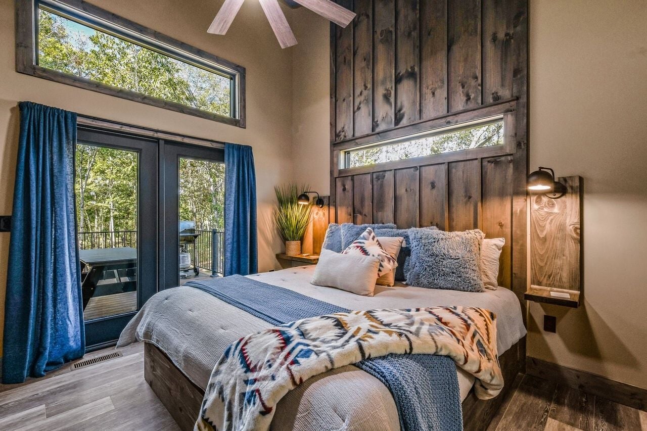 Quarto com uma cama grande, cabeceira de madeira e vista para o exterior por uma porta de correr.