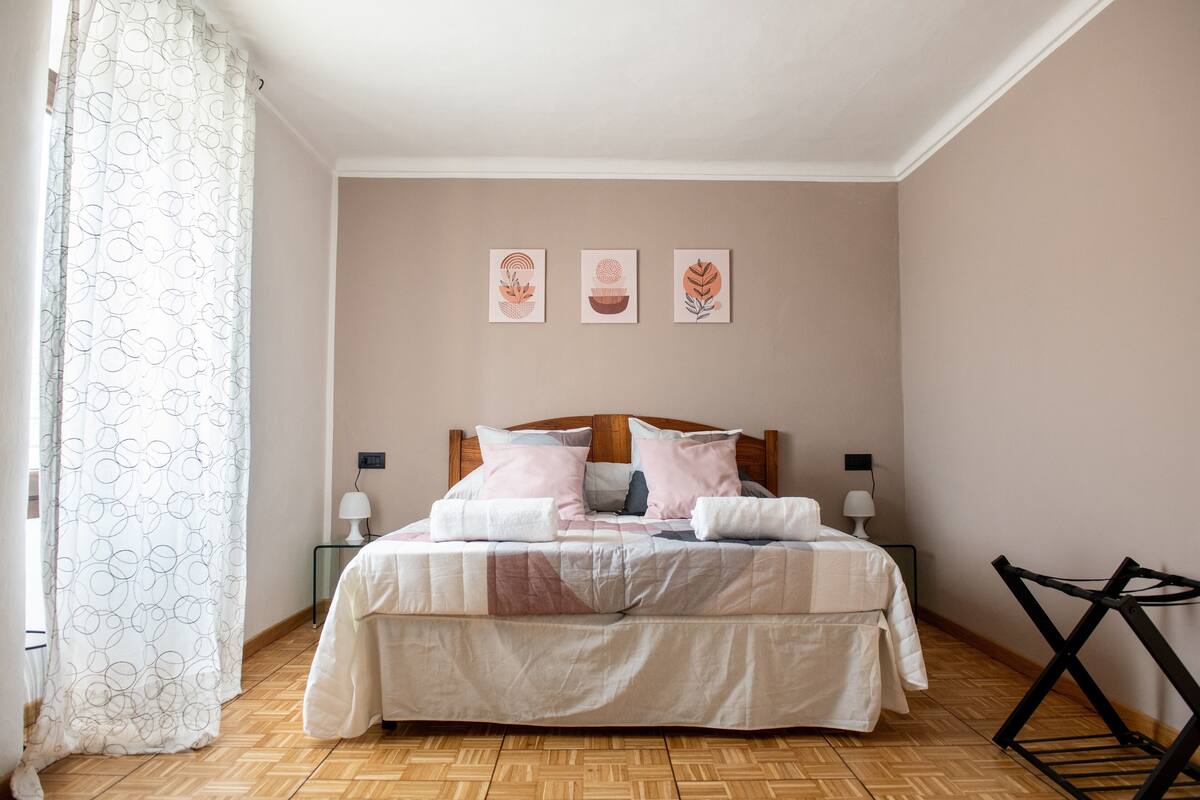 Uma cama bem arrumada com cabeceira de madeira, duas mesas de cabeceira com luminárias, e três obras de arte nas paredes acima da cama.