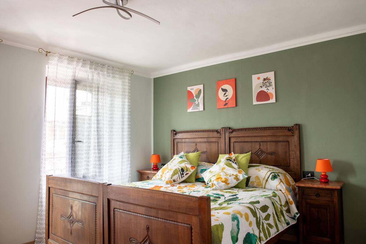 Quarto com cama de madeira, paredes verdes e duas mesas de cabeceira com abajures.