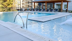 Piscina com trampolim, espreguiçadeiras e um edifício com varandas ao fundo.