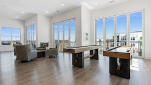 Uma sala de estar ampla com mesa de bilhar, assentos confortáveis e grandes janelas com vista para a cidade.