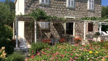 Um edifício de pedra com área externa coberta para sentar e um jardim com flores coloridas.