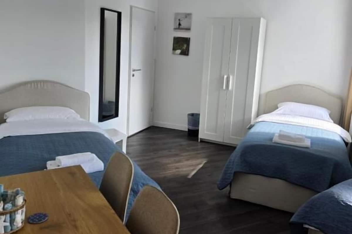 Quarto de hotel com duas camas, uma mesa de madeira e um guarda-roupa.