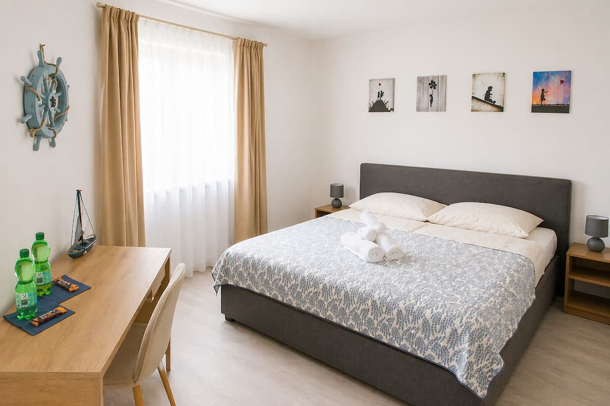 Quarto de hotel com cama, escrivaninha, cadeira, decoração de roda de navio e três quadros na parede.