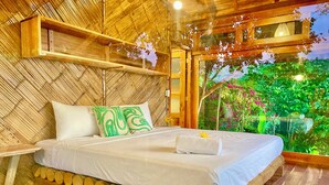 Uma cama com base de tronco de madeira, roupa de cama branca e almofadas verdes.