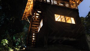 Uma cabana de madeira com escada em espiral, janelas amplas e telhado inclinado.