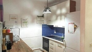 Uma cozinha compacta com micro-ondas, fogão e frigorífico. Há placas na parede e um candeeiro suspenso.