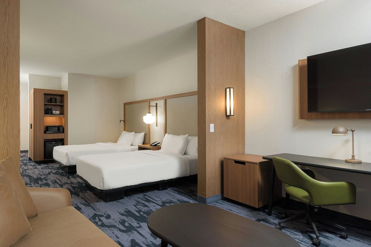 Quarto de hotel com duas camas, uma mesa, uma cadeira, uma televisão e um minibar.