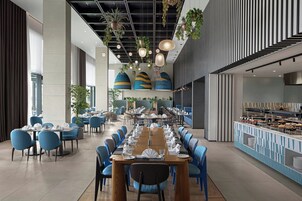 Uma sala de jantar ampla com várias mesas e cadeiras, um balcão de buffet e plantas penduradas.