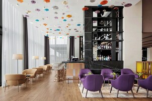 Uma área de bar moderna com um balcão comprido, banquetas e um espaço de estar com cadeiras roxas.