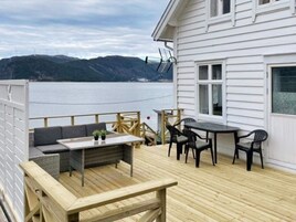 Um terraço com mesa e cadeiras, com vista para um corpo de água e colinas.