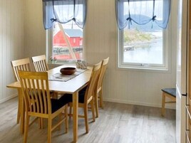 Uma área de jantar com mesa e cadeiras de madeira, uma tigela sobre a mesa, e uma janela com cortinas.