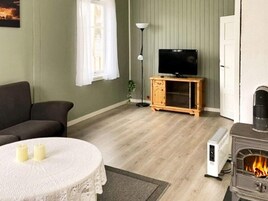 Uma sala de estar com sofá, televisão sobre um suporte de madeira, lareira e uma mesa com velas.