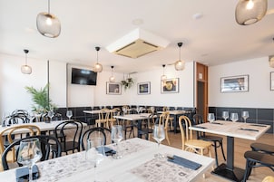 Interior de restaurante com várias mesas, cadeiras, luminárias pendentes e obras de arte nas paredes.