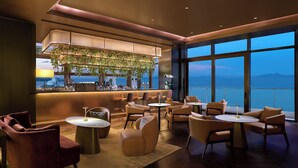 Um lounge moderno com assentos de couro, área de bar e amplas janelas com vista para o mar.