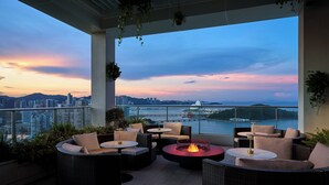 Terraço no telhado com mobiliário de vime, lareira e vista para a cidade e um corpo d'água.