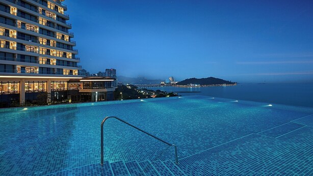 Um hotel com uma grande piscina infinita, vista para o mar e uma ilha ao longe.