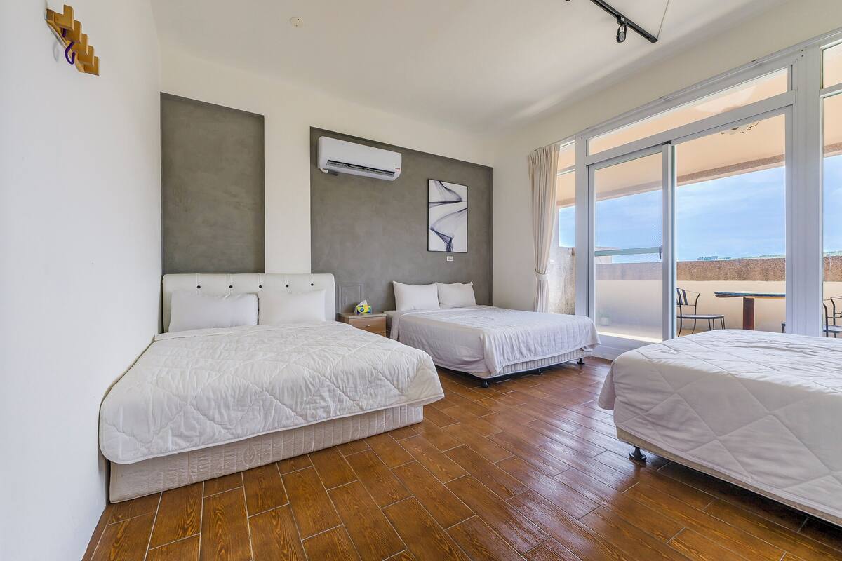 Quarto de hotel com duas camas, uma janela grande e vista para a praia.